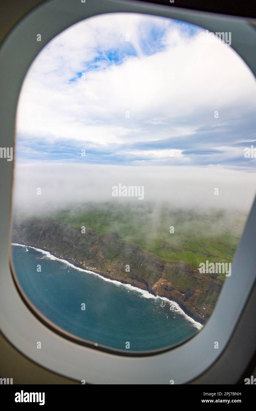 View to island from plane window, ocean, clouds and green fields Stock ...