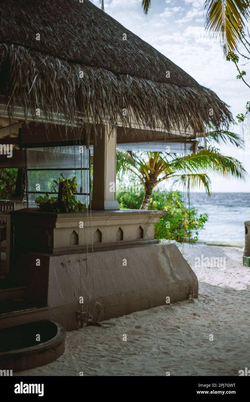 Sunny day at a sandy beach bar built on sandstone with a thatched roof ...