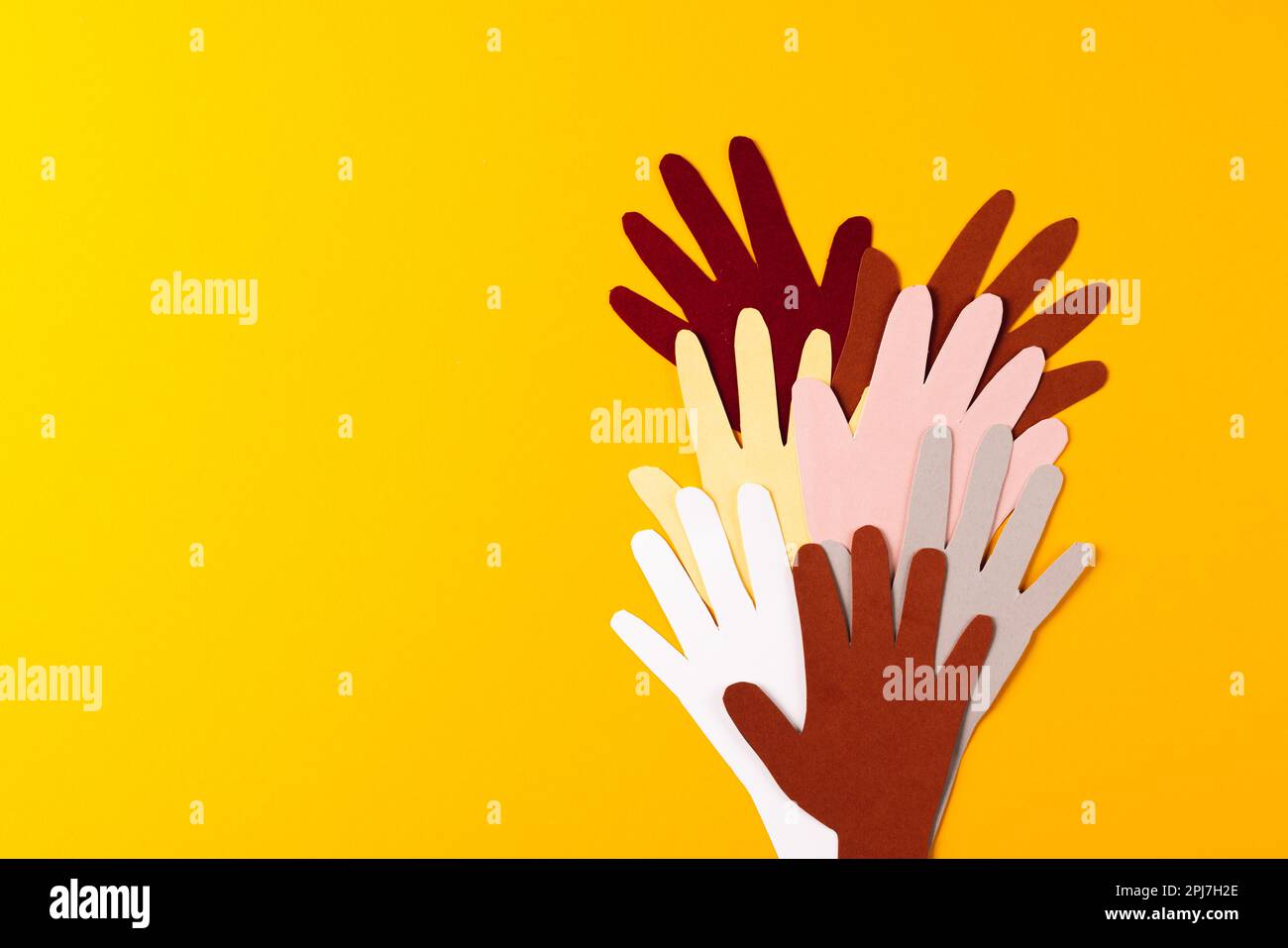 Paper cut out of multi coloured hands with copy space on orange ...