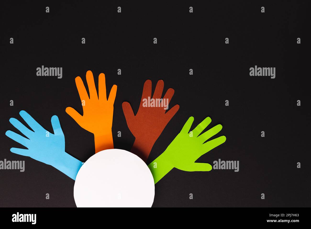 Paper cut out of multi coloured hands and white circle with copy space ...