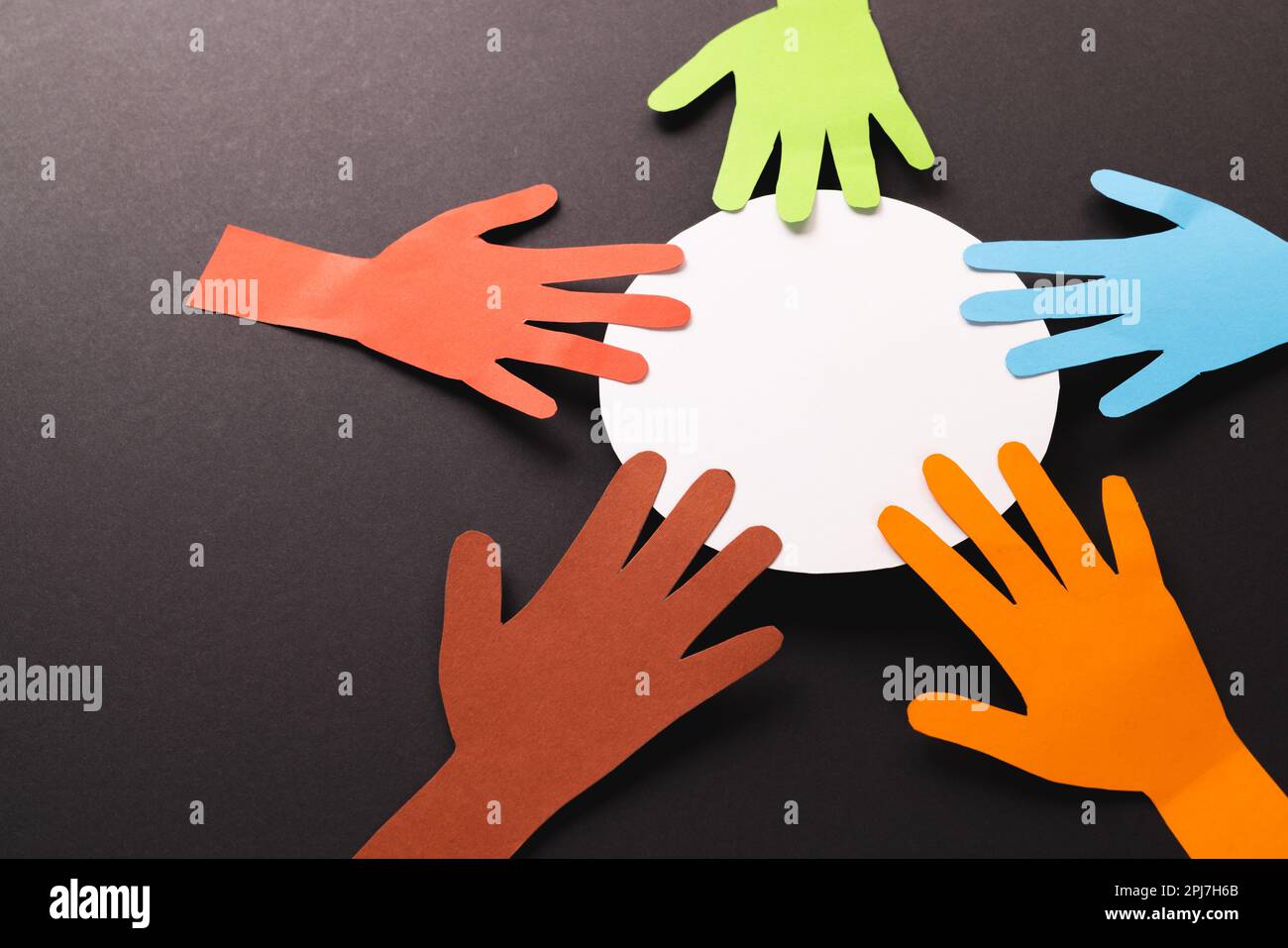 Paper cut out of multi coloured hands and white circle with copy space ...