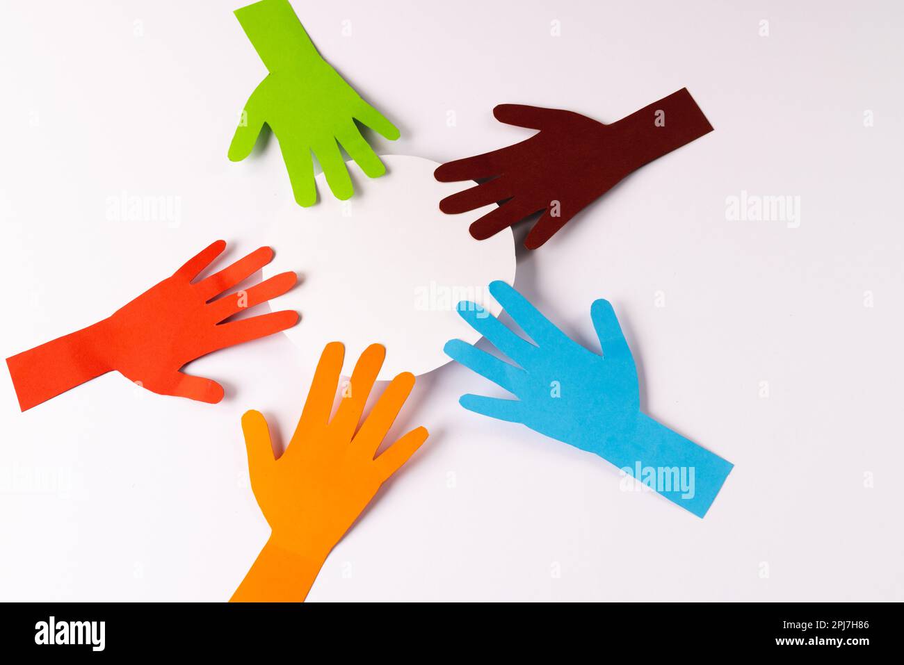 Paper cut out of multi coloured hands and white circle with copy space ...
