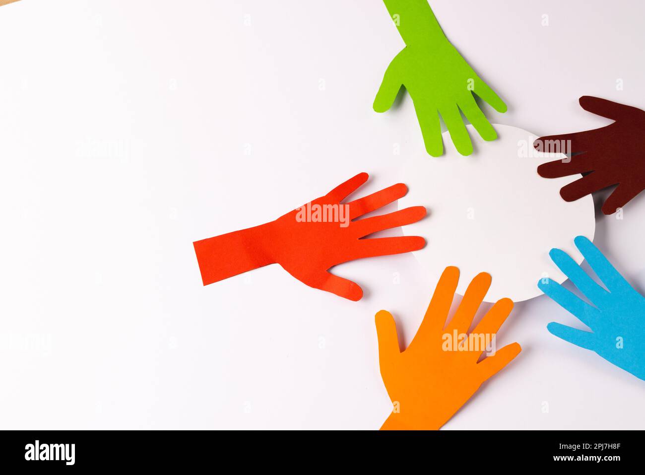Paper cut out of multi coloured hands and white circle with copy space ...