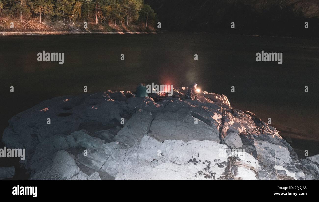 Two women sit on the bank of the Katun River near the fire and fish ...