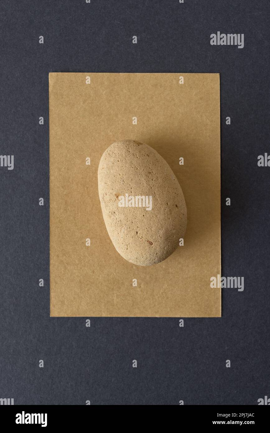 ovoid shaped brick pebble isolated on gold or sand brown card and grey ...