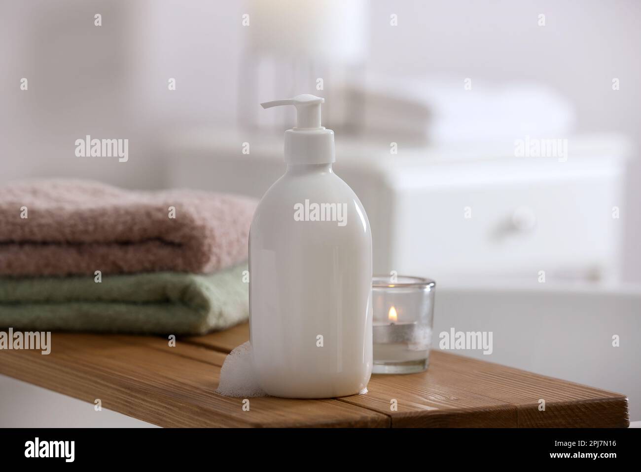 Bottle of bubble bath with foam, towels and candle on tub in bathroom ...