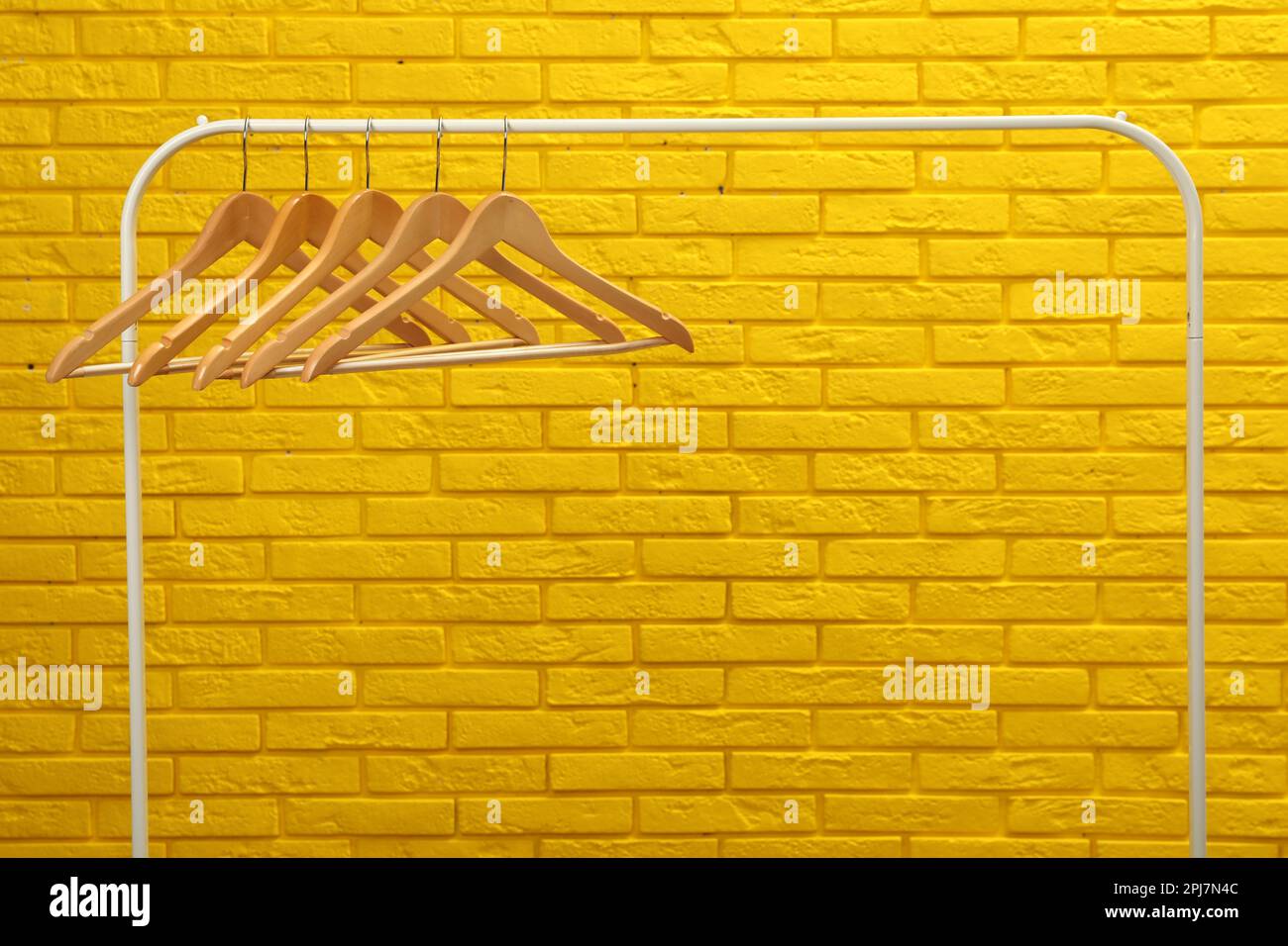 Wardrobe rack with many hangers near yellow brick wall Stock Photo - Alamy