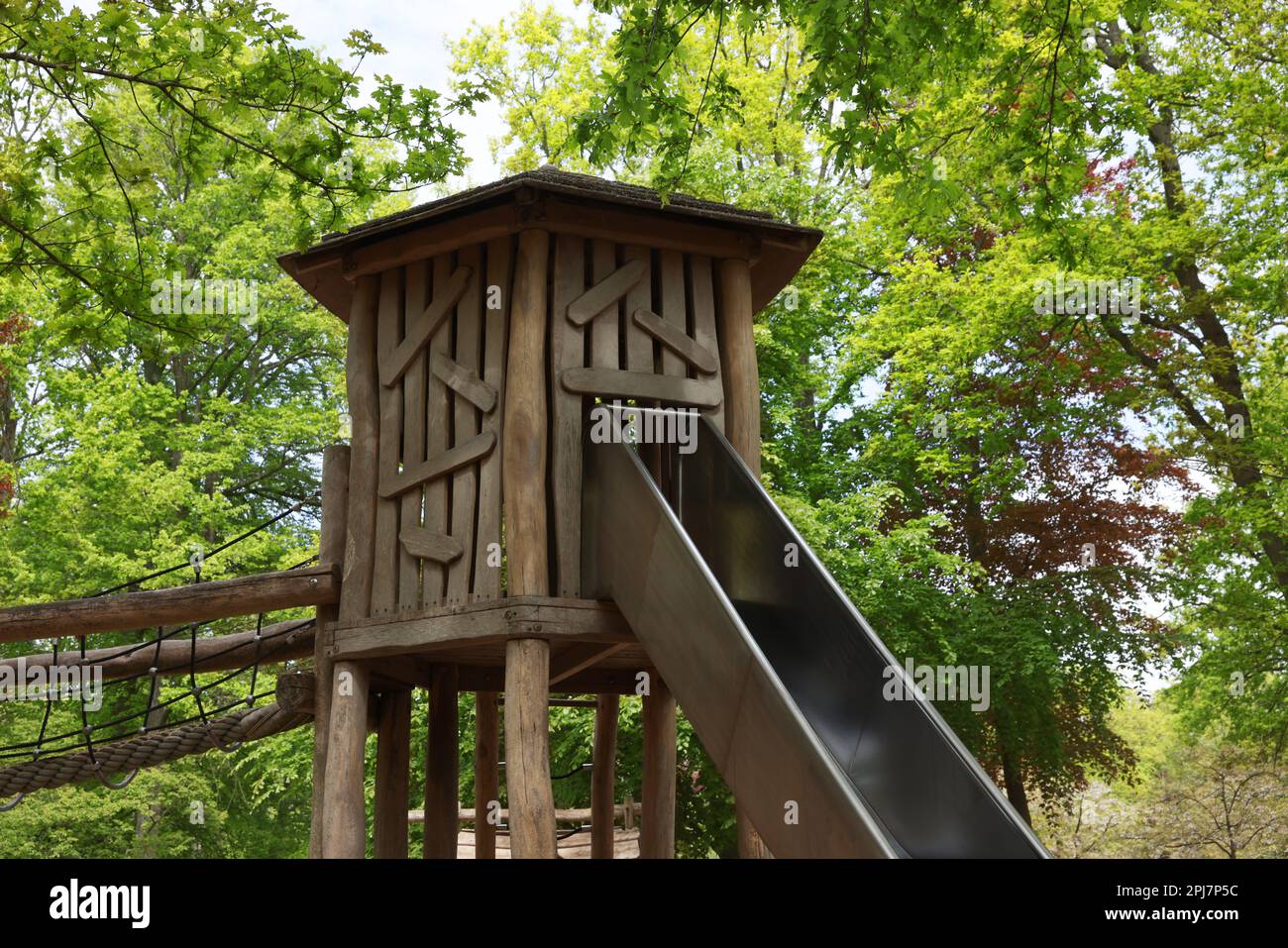 Wooden slide with bridge near big trees in park. Outdoor playground ...