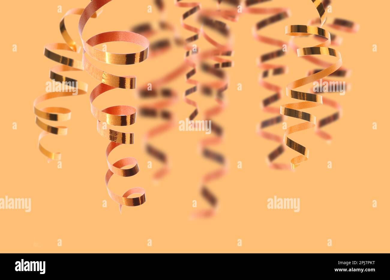 Many golden serpentine streamers on pale orange background. Party decor ...