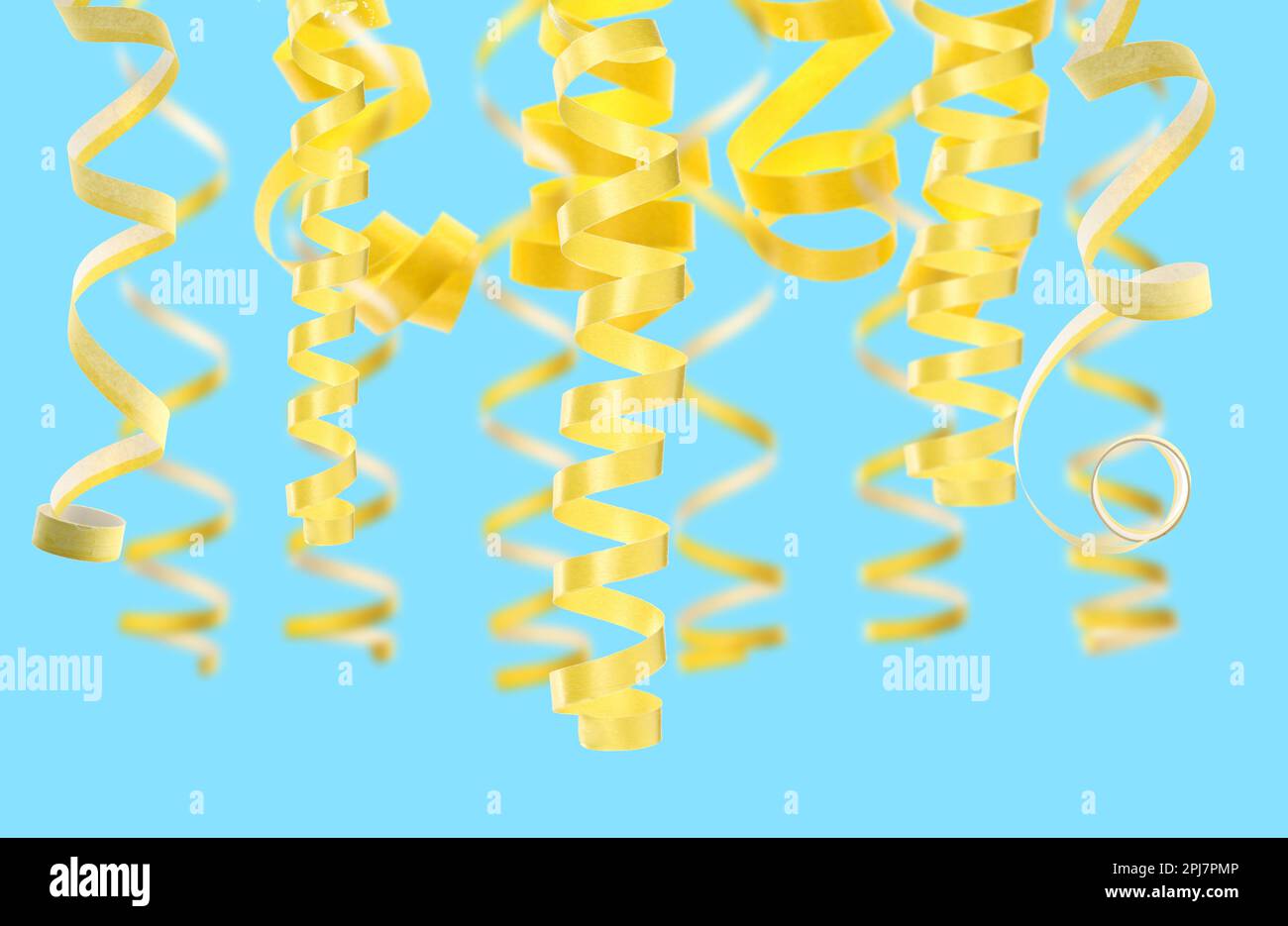 Many yellow serpentine streamers on light blue background. Party decor ...