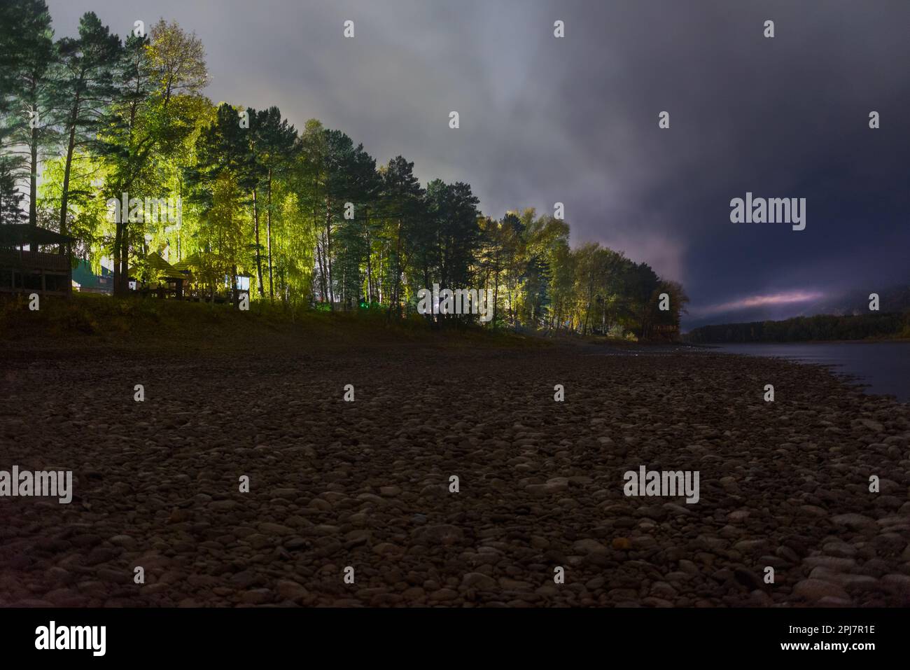 Mountain stone bank of the Katun River with trees at night illuminated ...