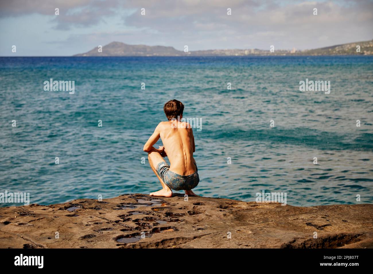 Oahu, Hawaii, USA, - February 7, 2023: A young surfer boy squatting on ...