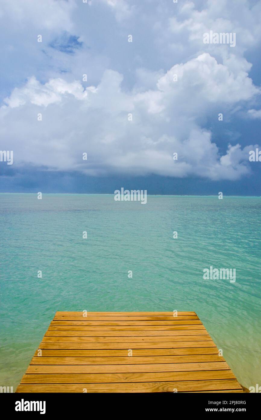 A dock in Aitutaki island Lagoon looking out on an approaching dark sky ...