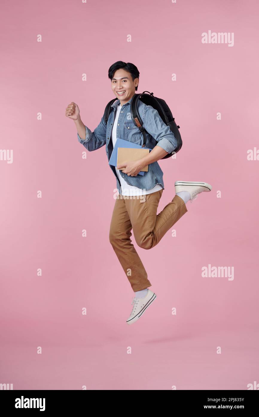 Full length portrait of a funny cheerful male student jumping on pink ...