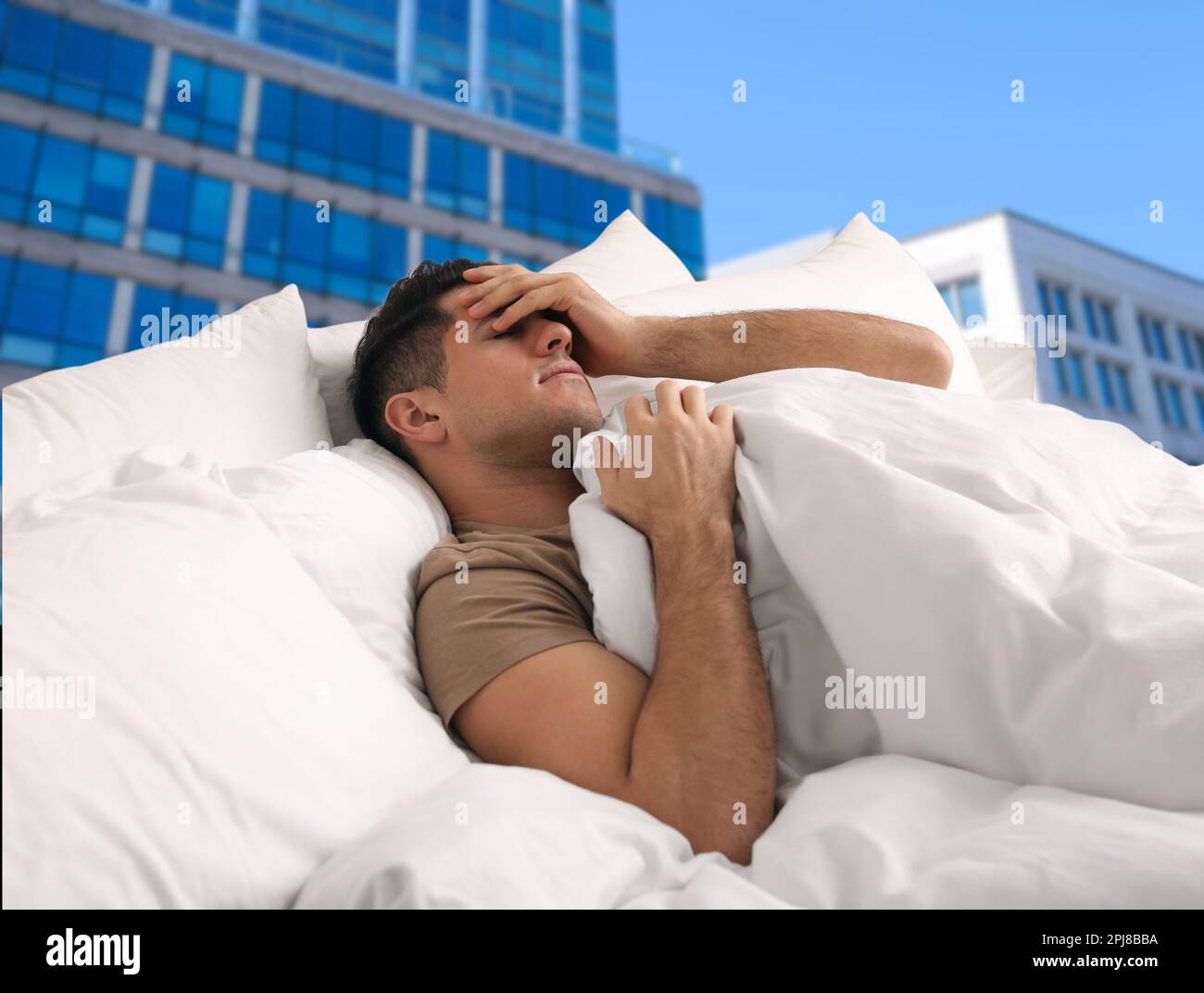 Man in bed and beautiful view of cityscape on background. Poor sleep ...