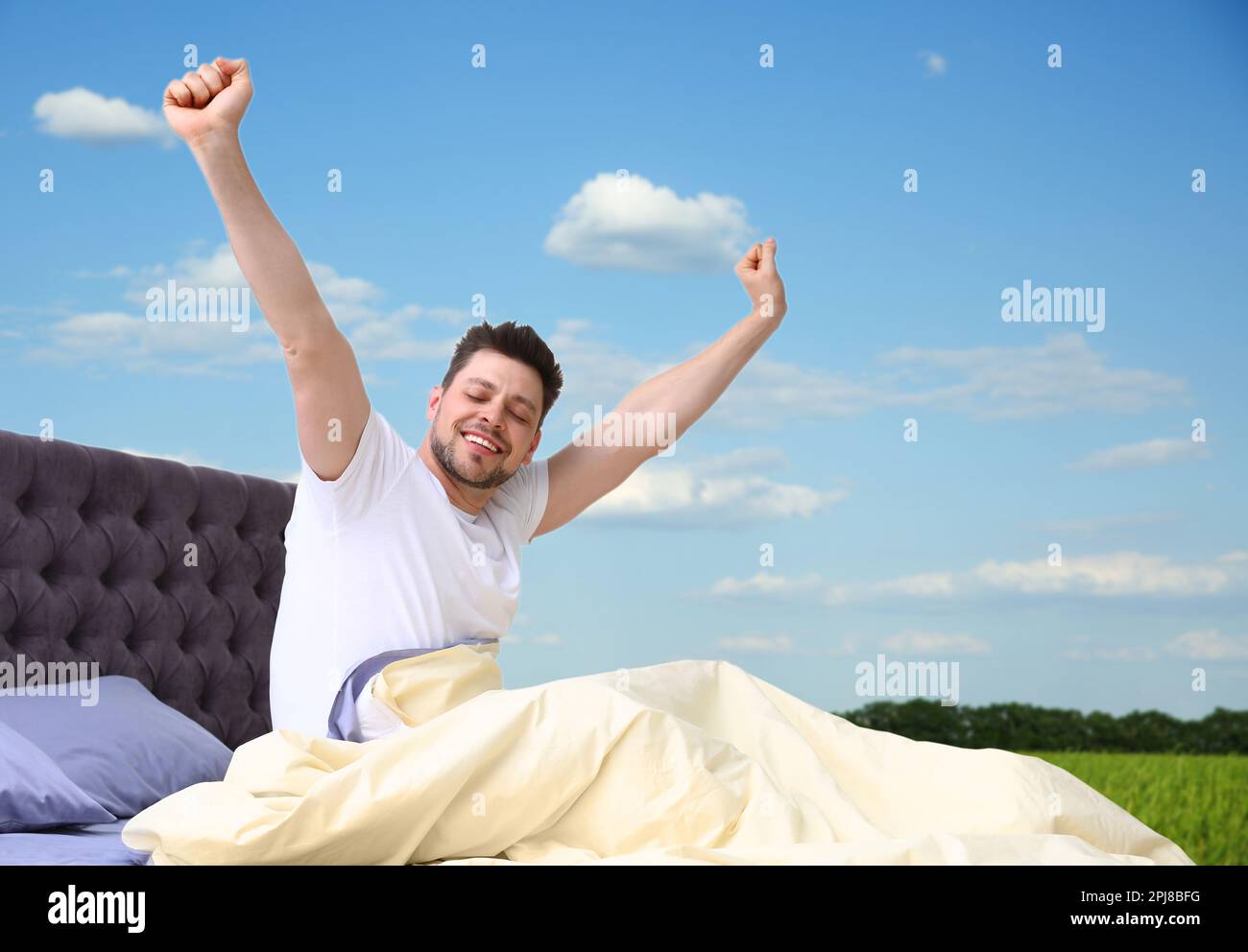 Happy man stretching in bed and beautiful view of green field on ...