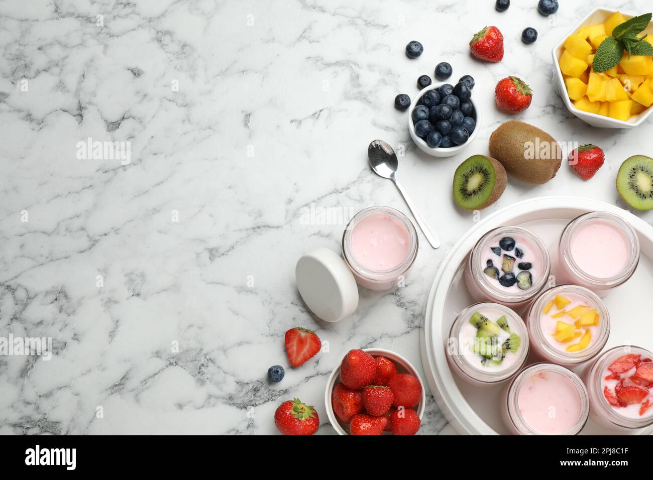 Modern yogurt maker with full jars and different fruits on white marble ...