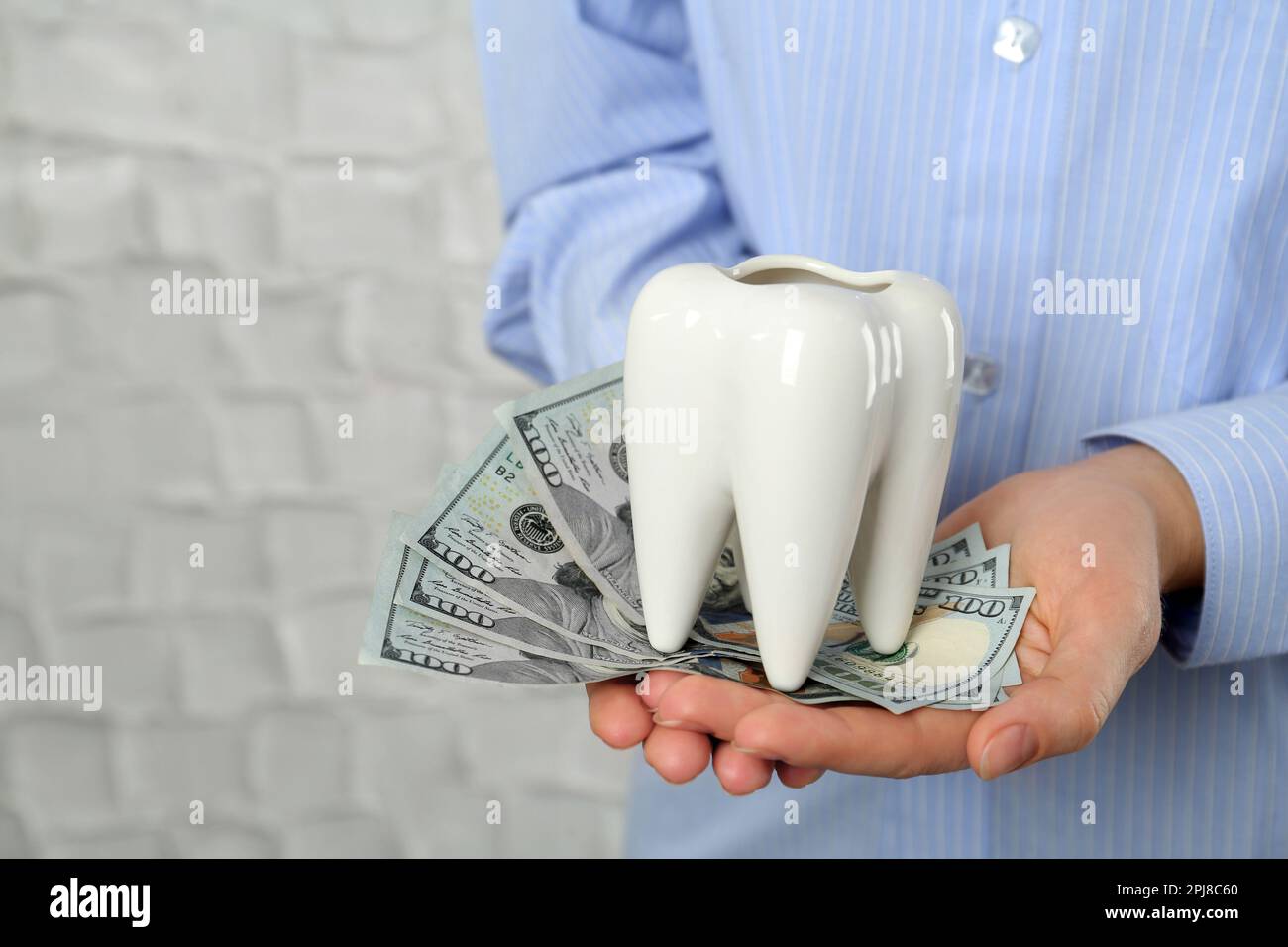 Woman holding ceramic model of tooth and dollar banknotes on light ...