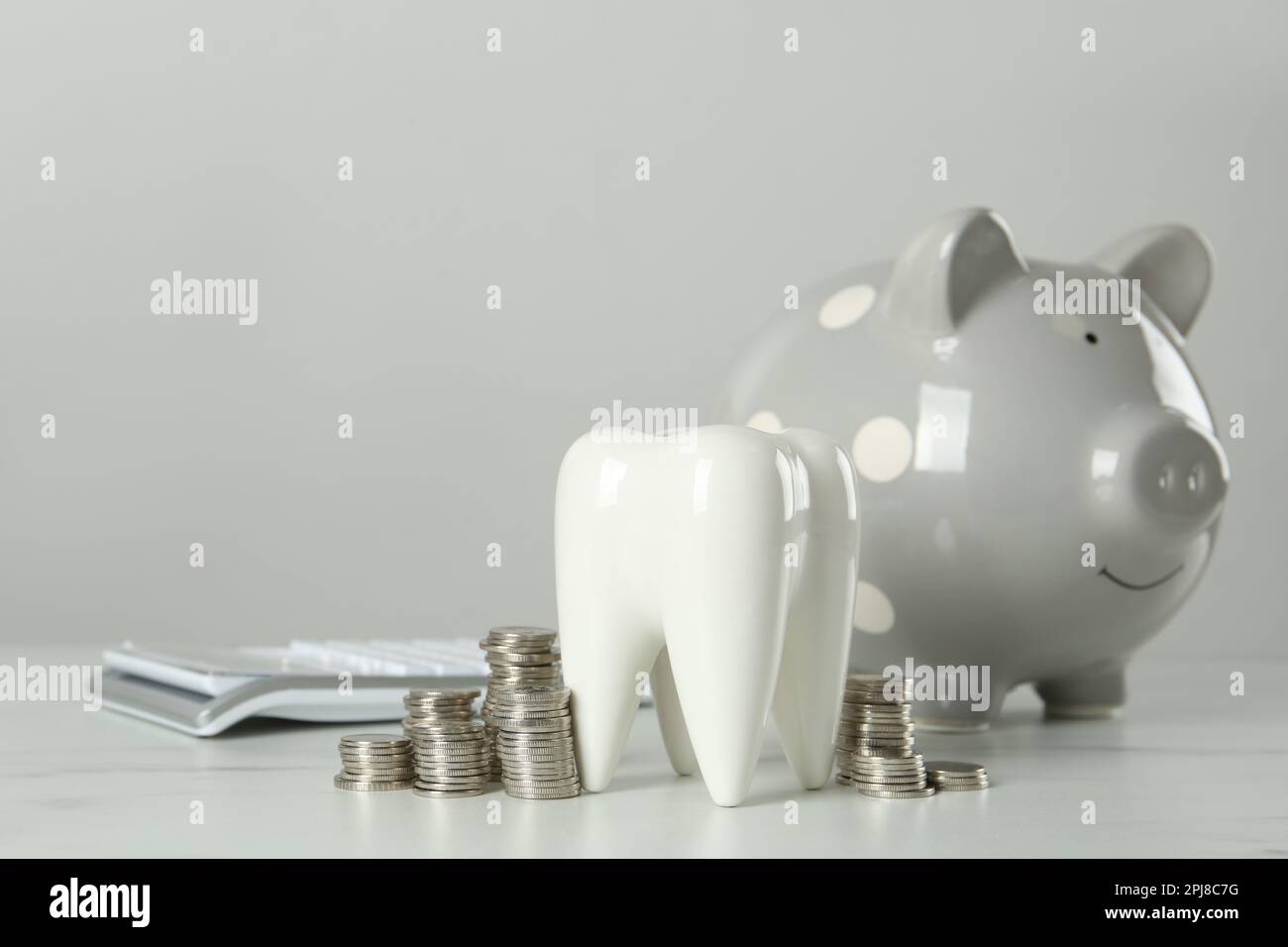 Ceramic model of tooth, piggy bank and coins on white table. Expensive ...
