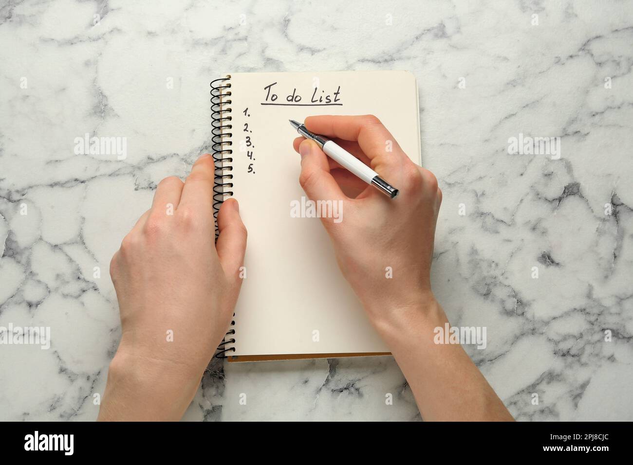 Woman filling To Do list in notepad at white marble table, top view ...