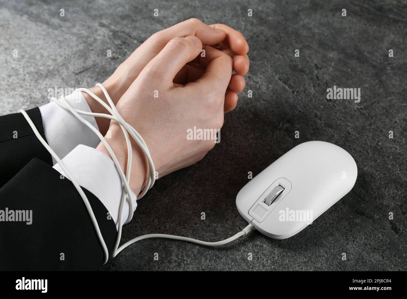 Man showing hands tied with computer mouse cable at grey table, closeup ...