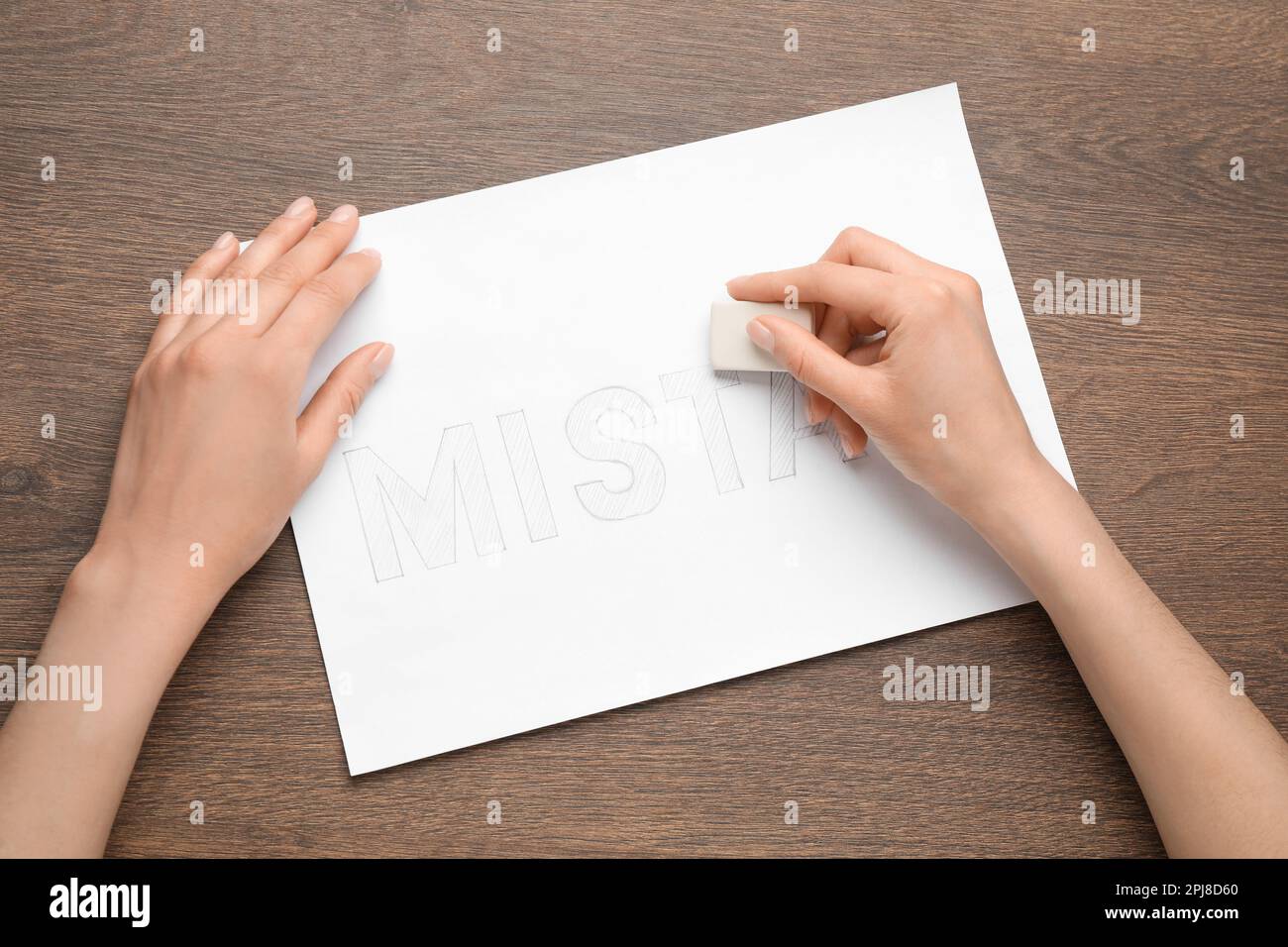 Woman erasing word on sheet of white paper at wooden table, top view ...