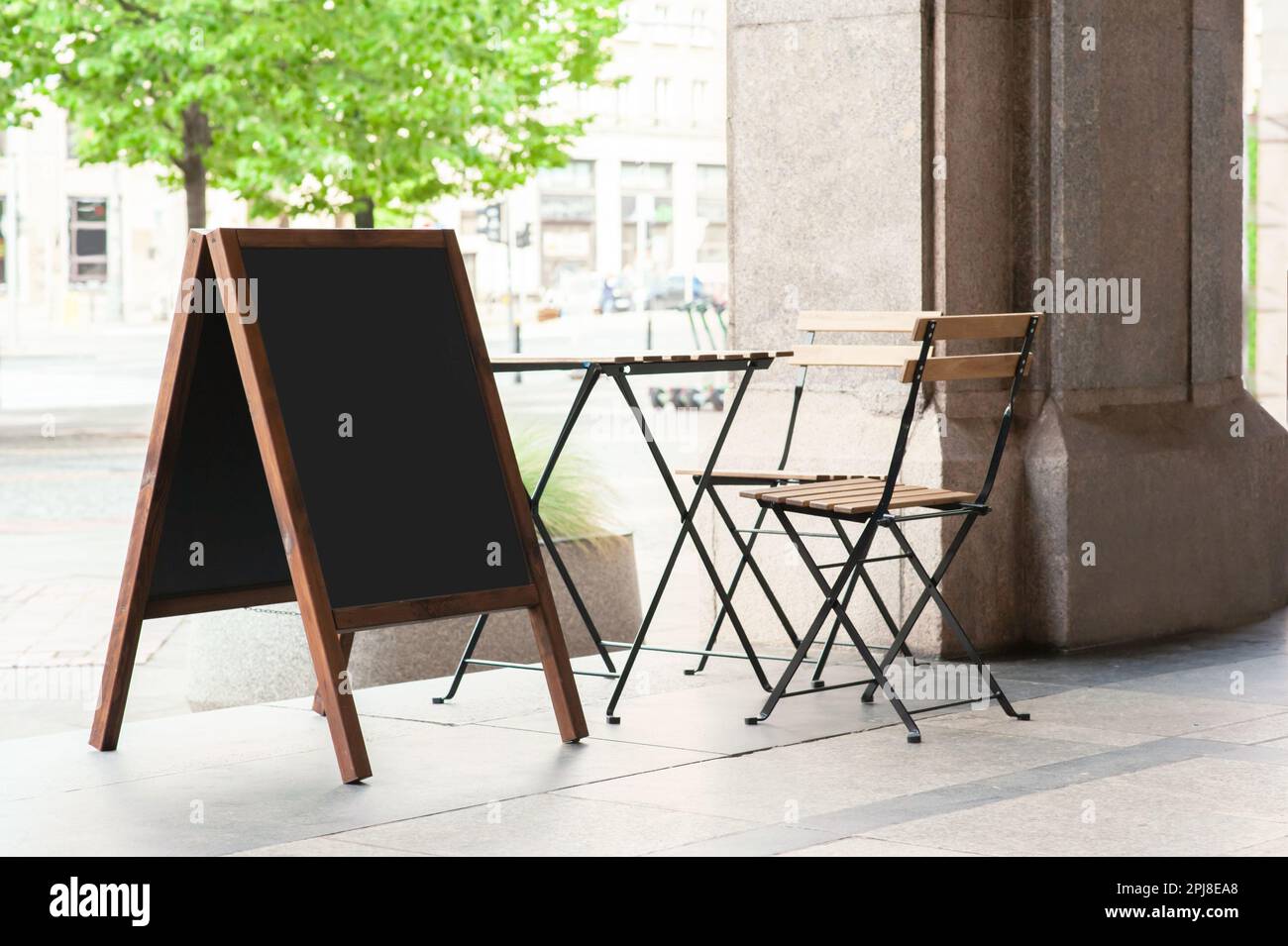 Blank wooden sandwich board near chair and table outdoors. Mockup for ...