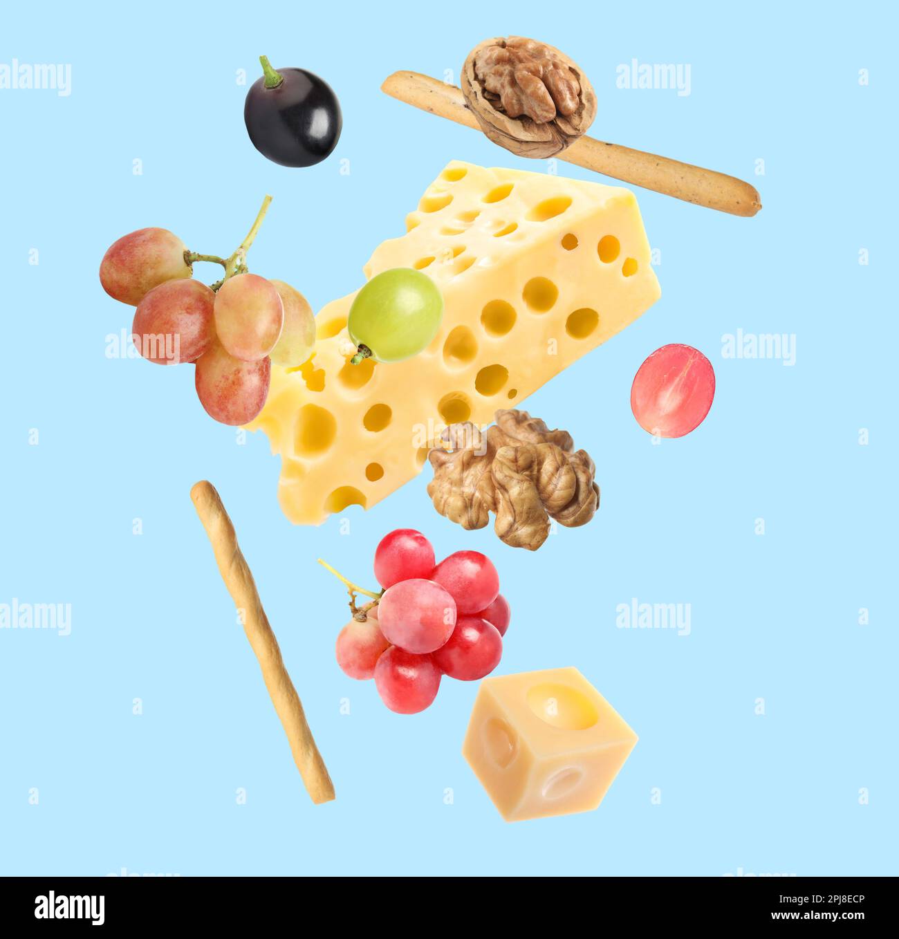 Cheese, breadsticks, grapes and walnuts falling against pale light blue ...