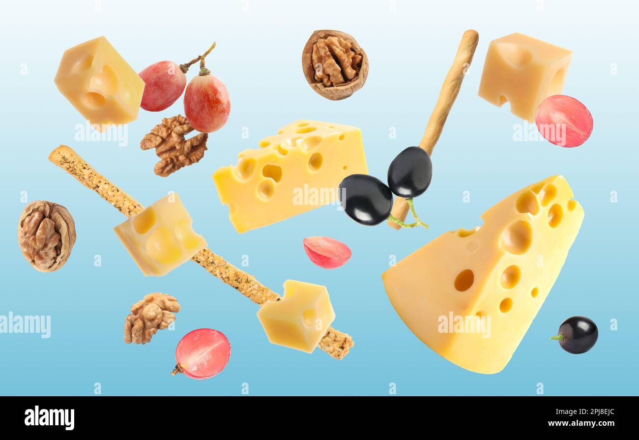 Cheese, breadsticks, grapes and walnuts falling against light blue ...