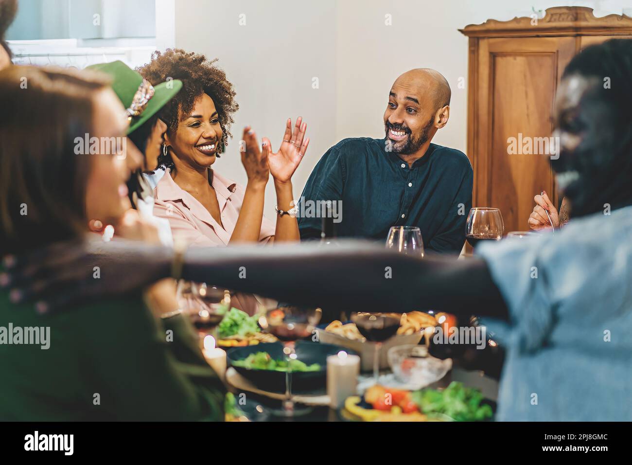Adult friends of various ethnicities are gathered around a dinner table ...