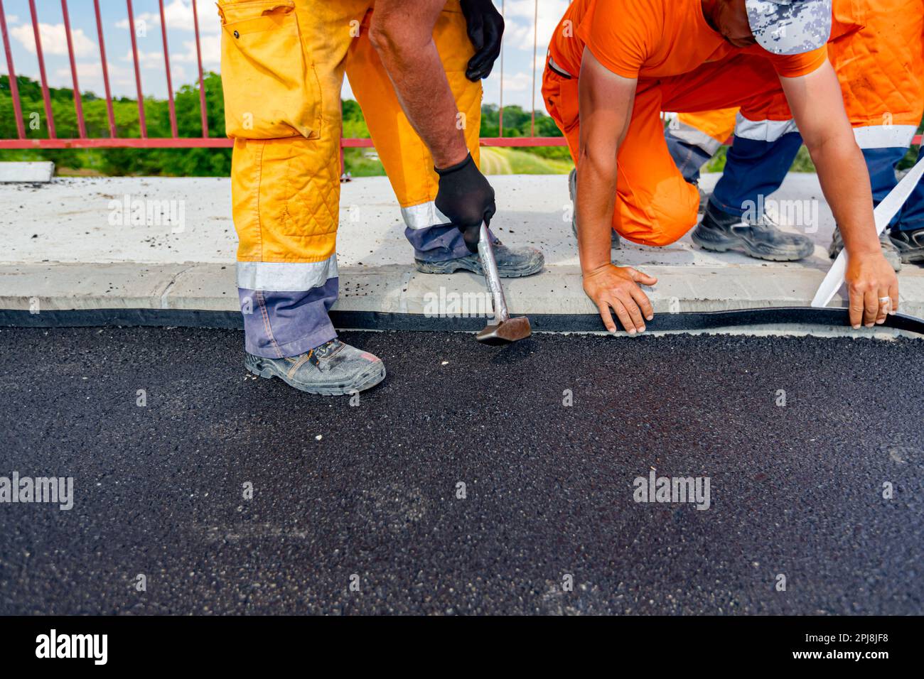Workers attach a bitumen black tape to protect the roadside of bridge ...