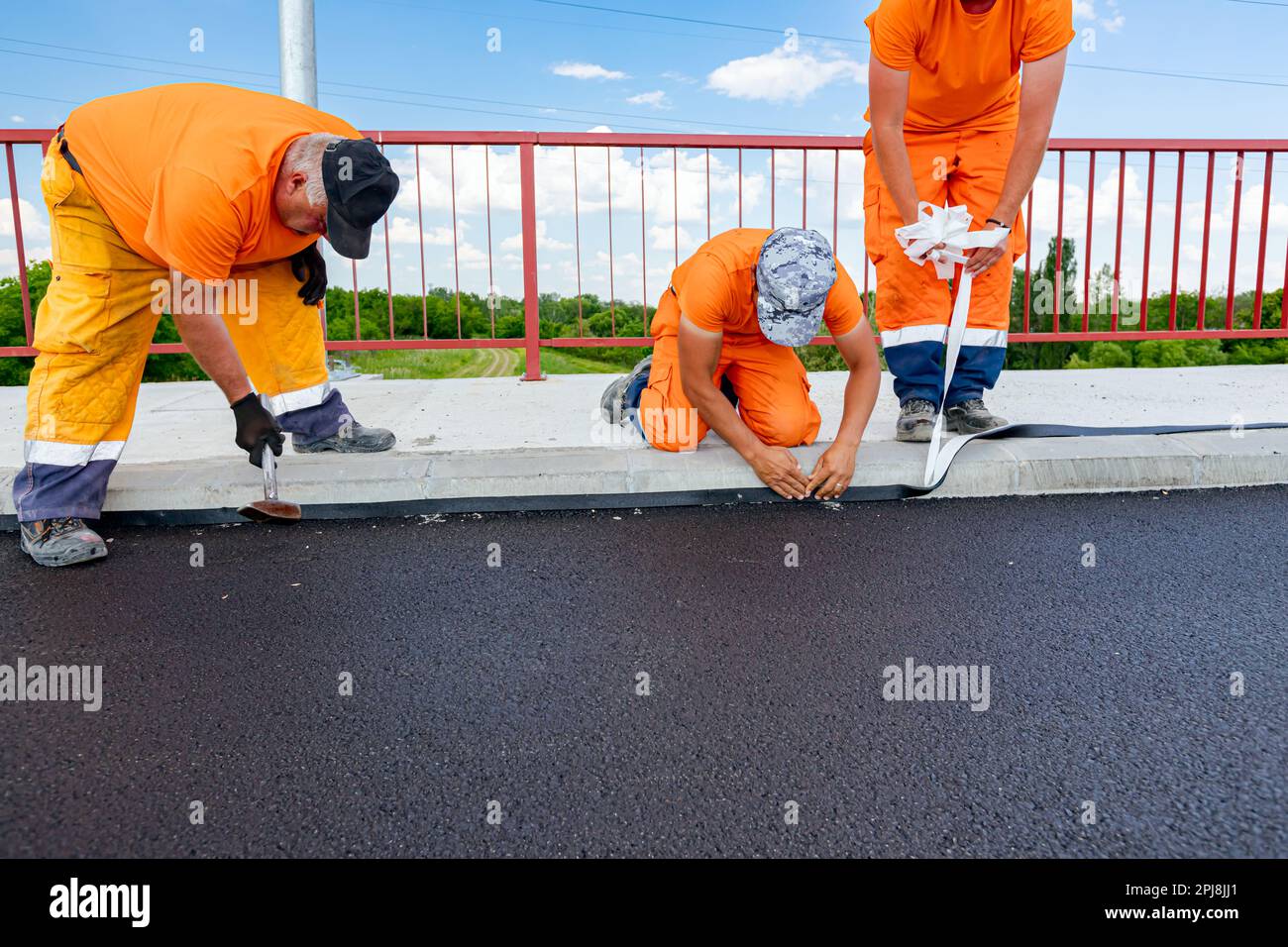 Workers attach a bitumen black tape to protect the roadside of bridge ...