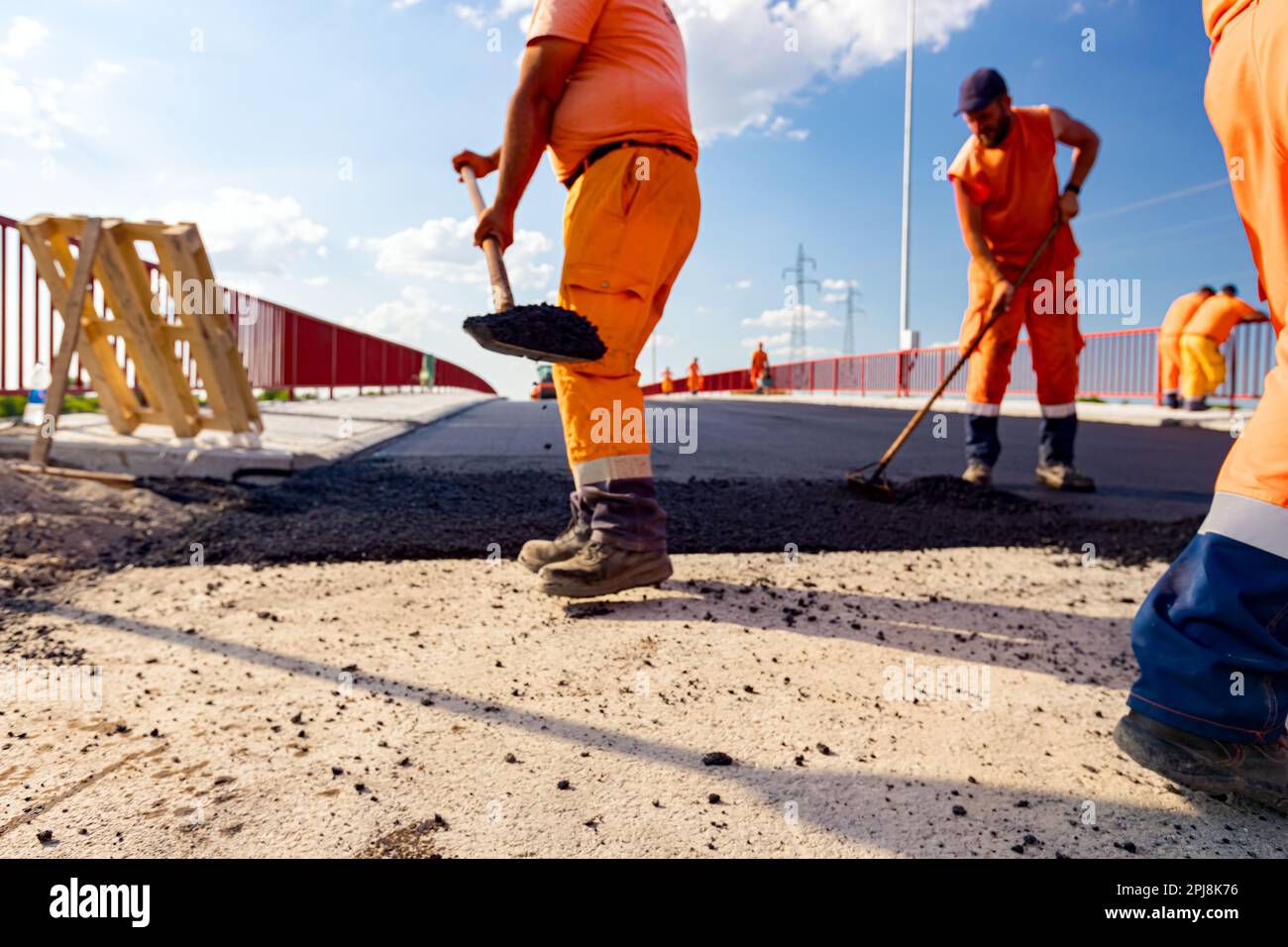 Few workers are using shovels to level, set up layer of fresh tarmac to ...