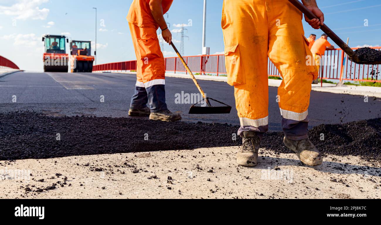 Few workers are using shovels to level, set up layer of fresh tarmac to ...