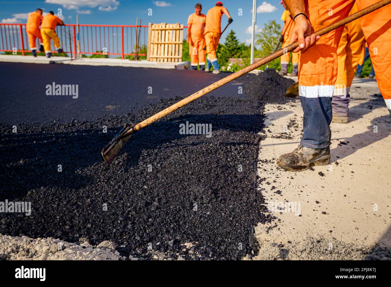 Few workers are using shovels to level, set up layer of fresh tarmac to ...