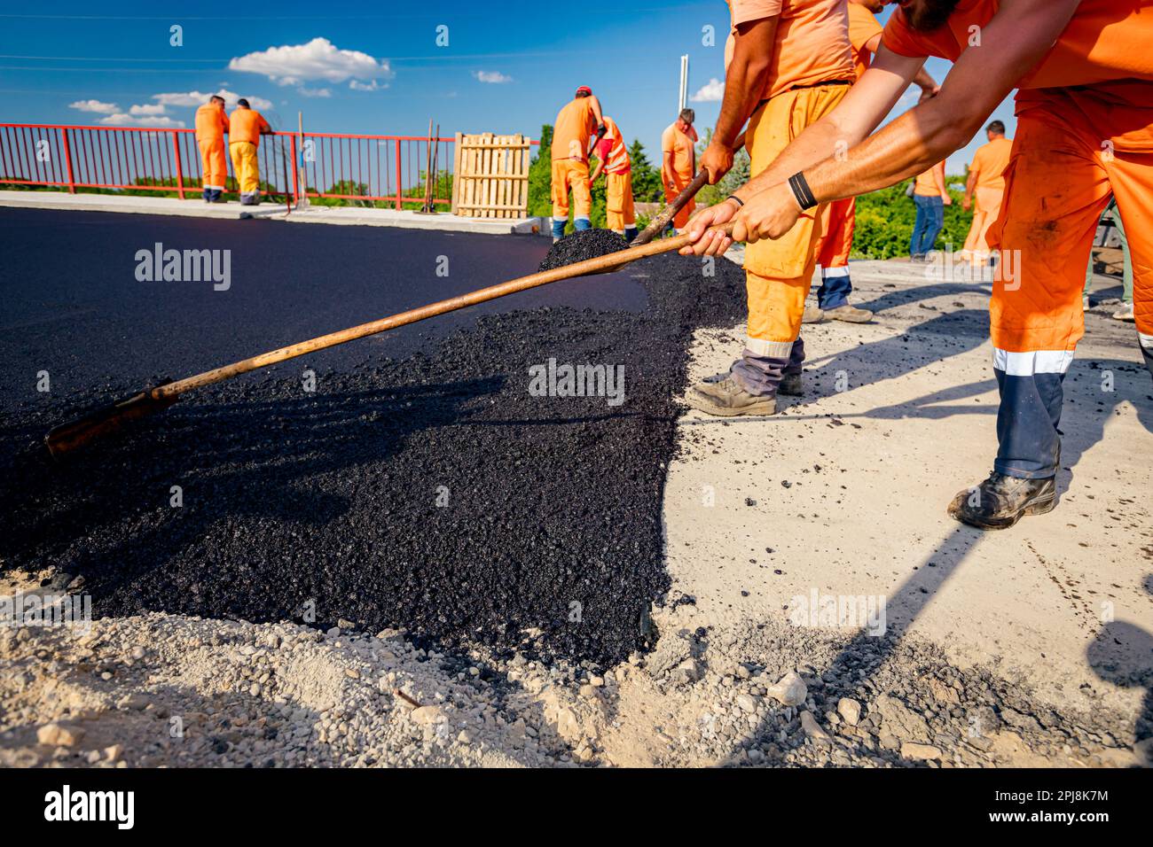 Few workers are using shovels to level, set up layer of fresh tarmac to ...