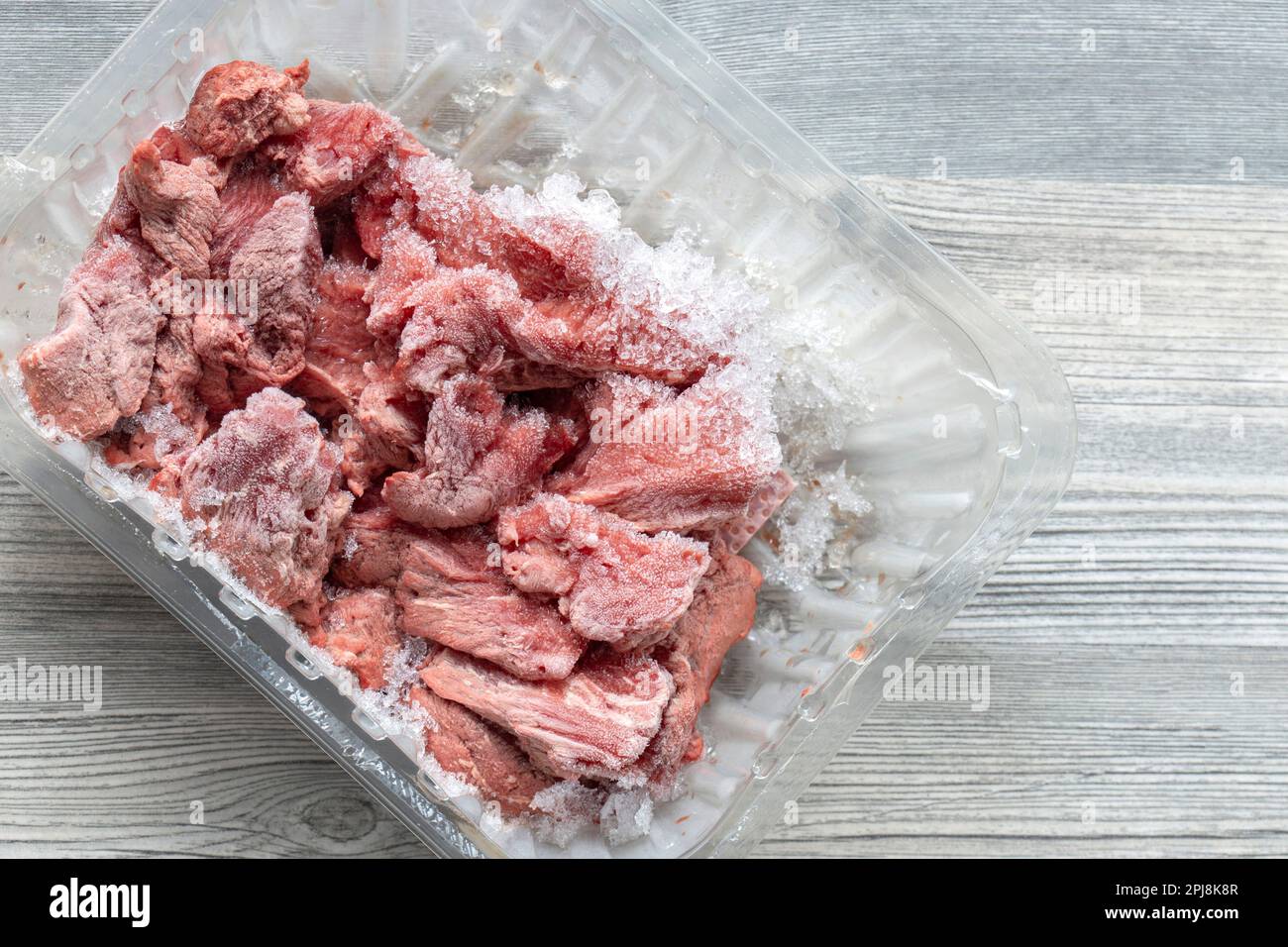 Frozen lean beef steak cubes in clear plastic tray packaging. On a grey ...