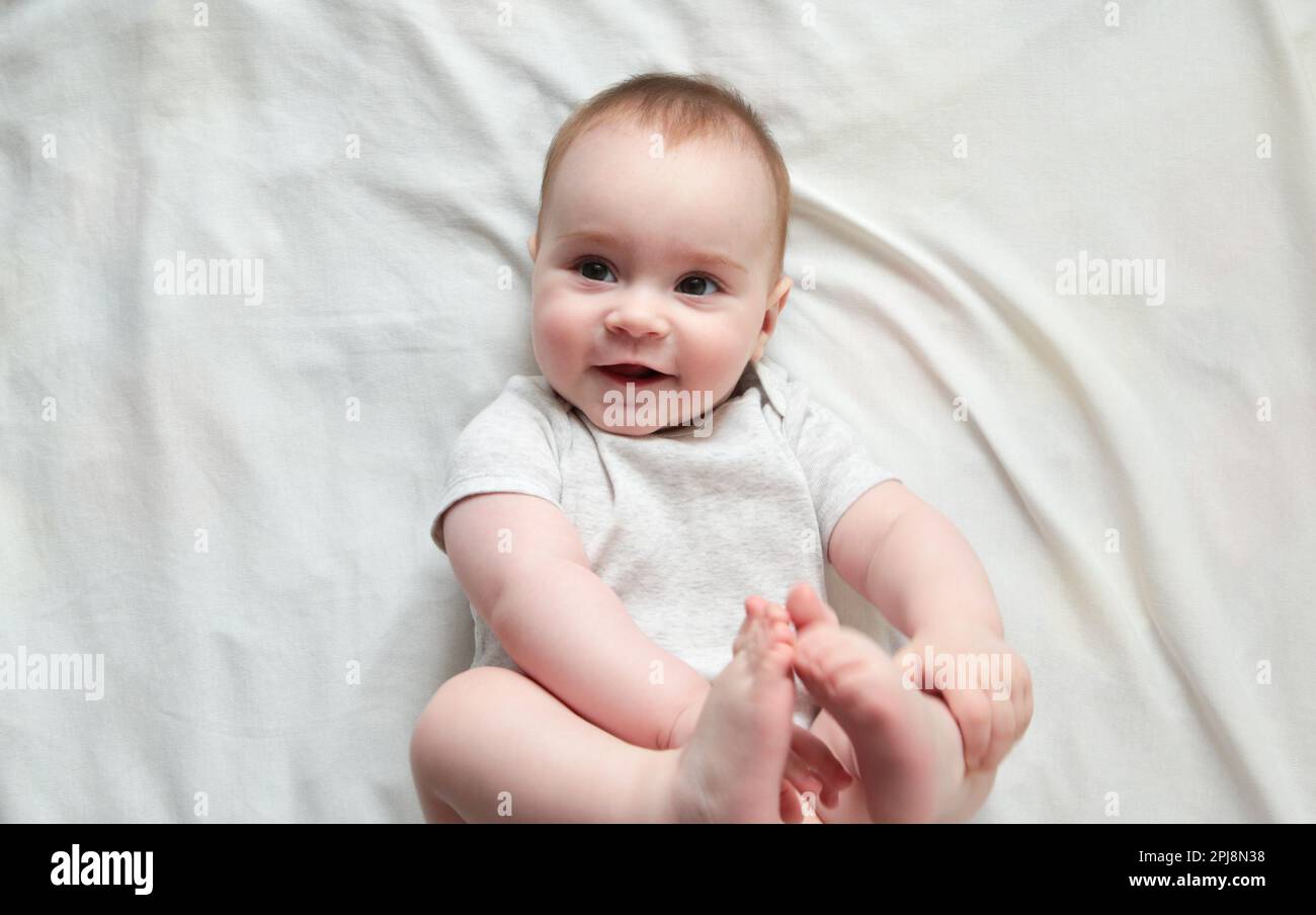 Cute baby lying and holding her legs on white bed, top view Stock Photo - Alamy