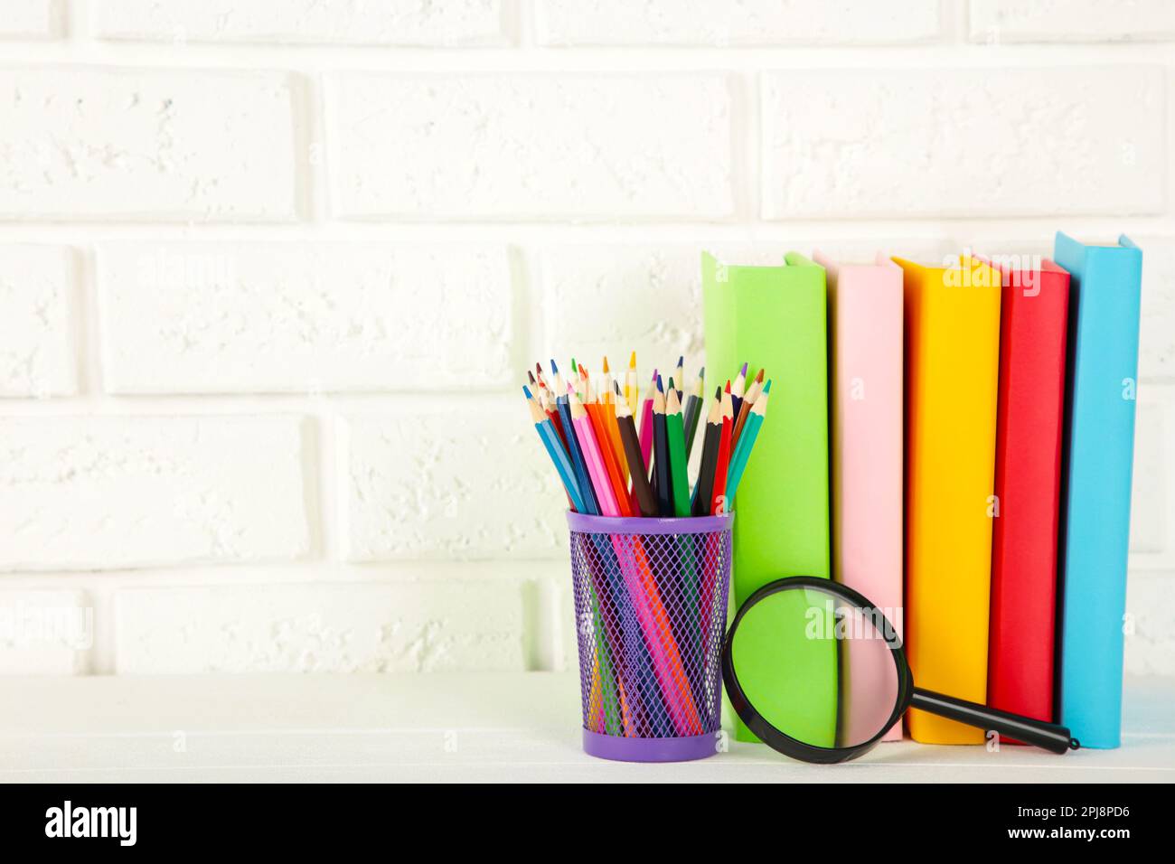 Multi coloured school books and stationery on white brick wall background. Copy space Stock ...