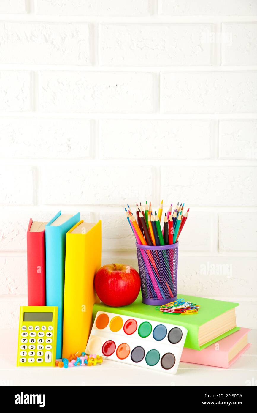 Multi coloured school books and stationery on white brick wall ...