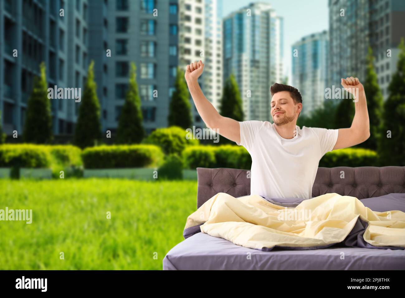 Happy man stretching in bed and beautiful view of green grass and ...