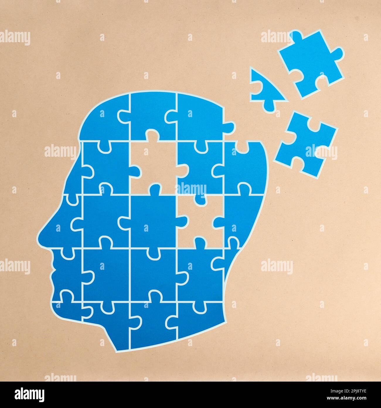 Dementia concept. Drawing of blue head shaped jigsaw puzzle with missing pieces on beige ...