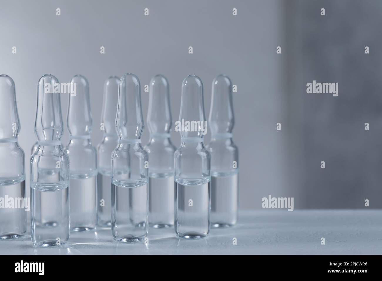Pharmaceutical ampoules with medication on white table against grey ...