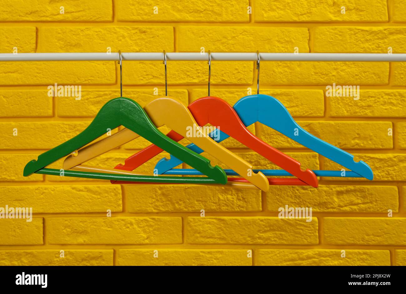 Wardrobe rack with many hangers near yellow brick wall Stock Photo - Alamy