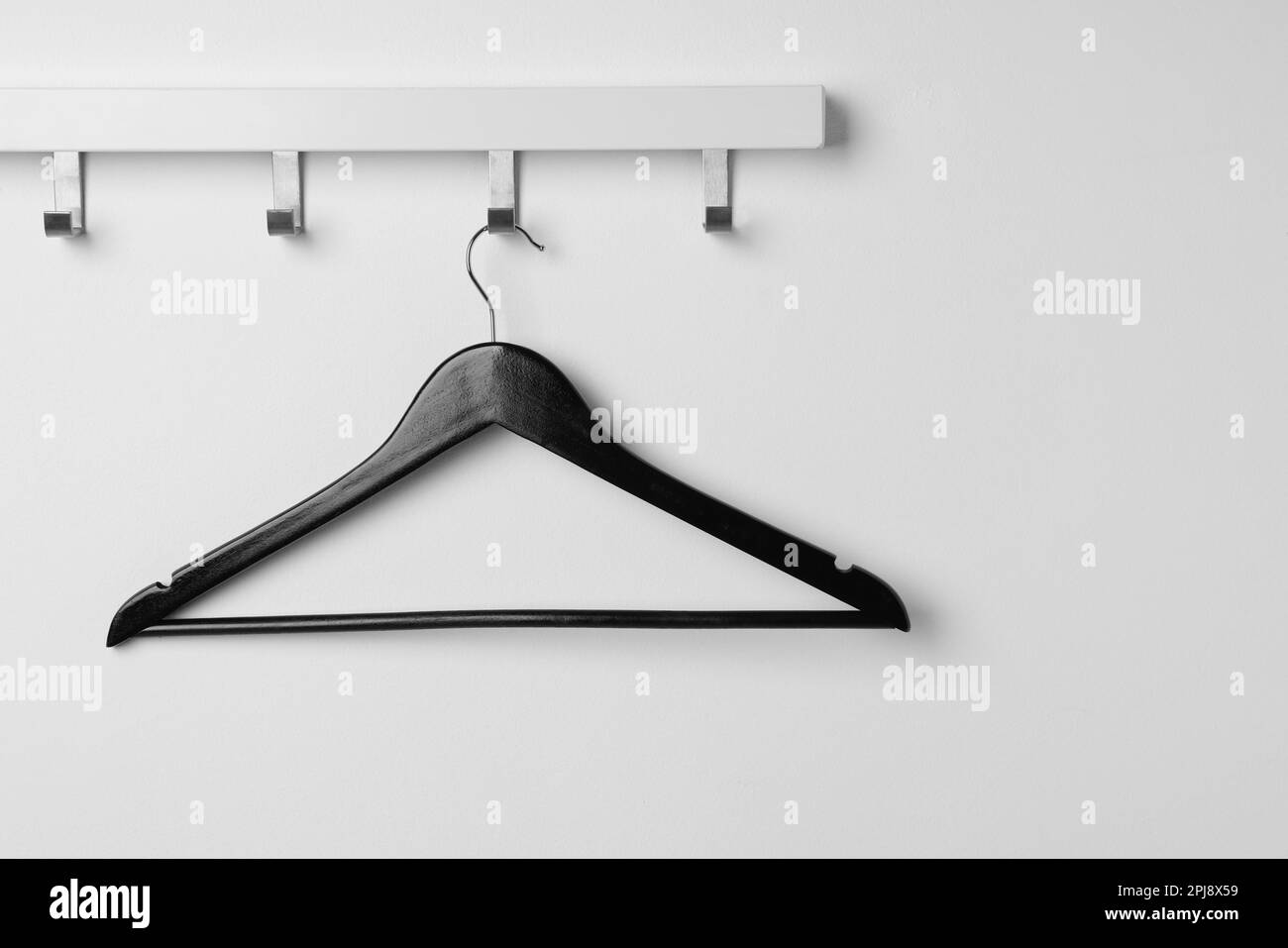 Rack with empty black clothes hanger on white wall Stock Photo - Alamy