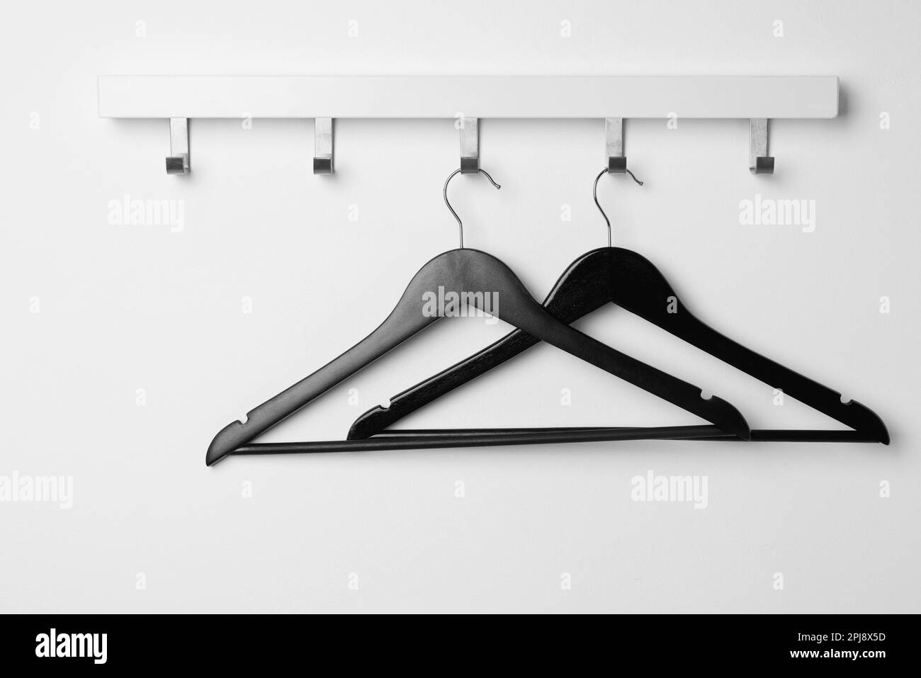Rack with empty black clothes hanger on white wall Stock Photo - Alamy