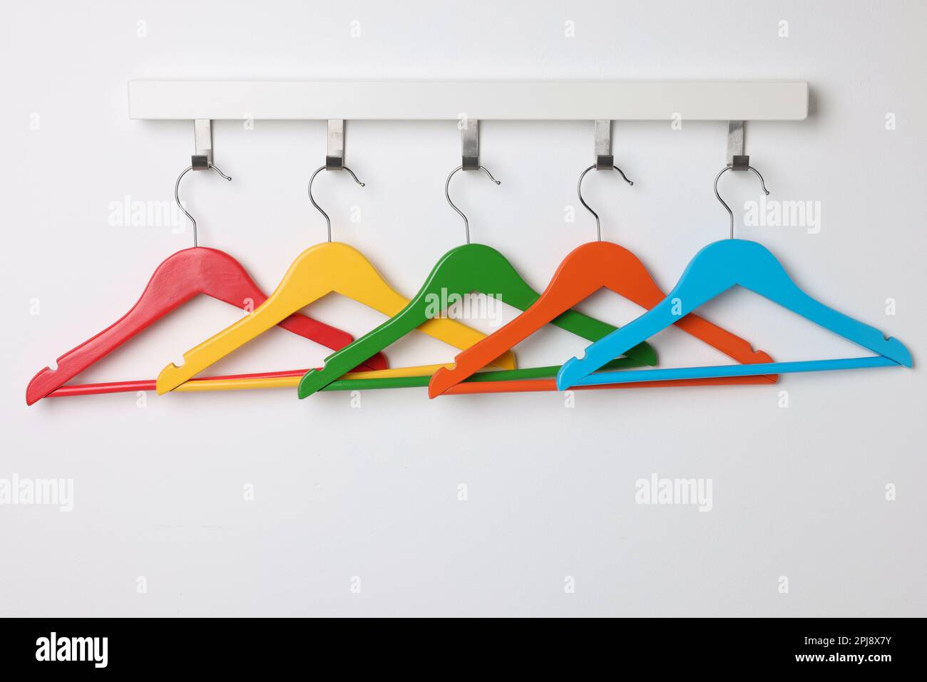 Rack with empty bright clothes hangers on white wall Stock Photo - Alamy