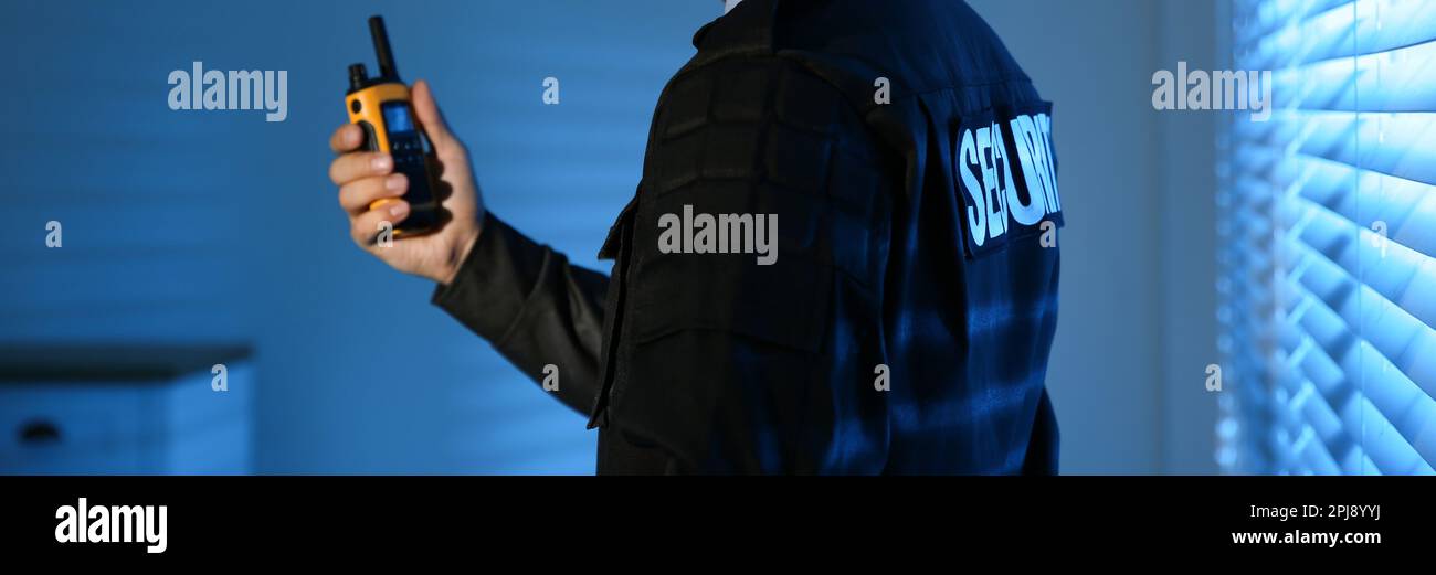 Professional security guard with portable radio set near window in dark ...