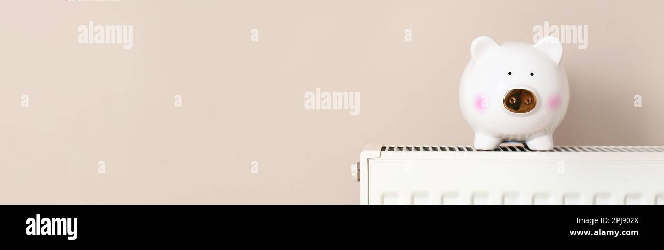 Piggy bank on heating radiator near light wall, space for text. Banner ...