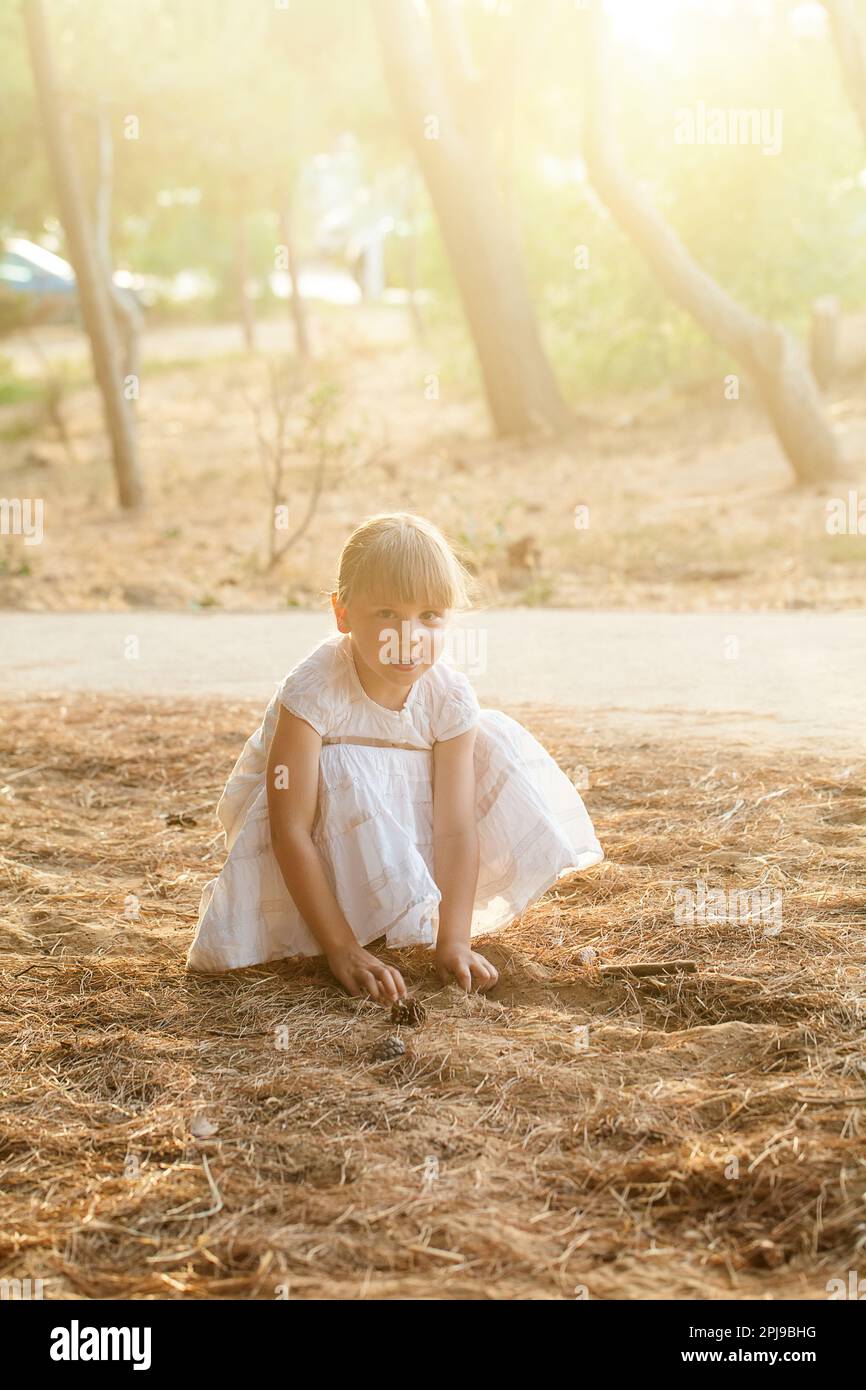 Child girl in white clothes playing on the ground in the park Stock ...